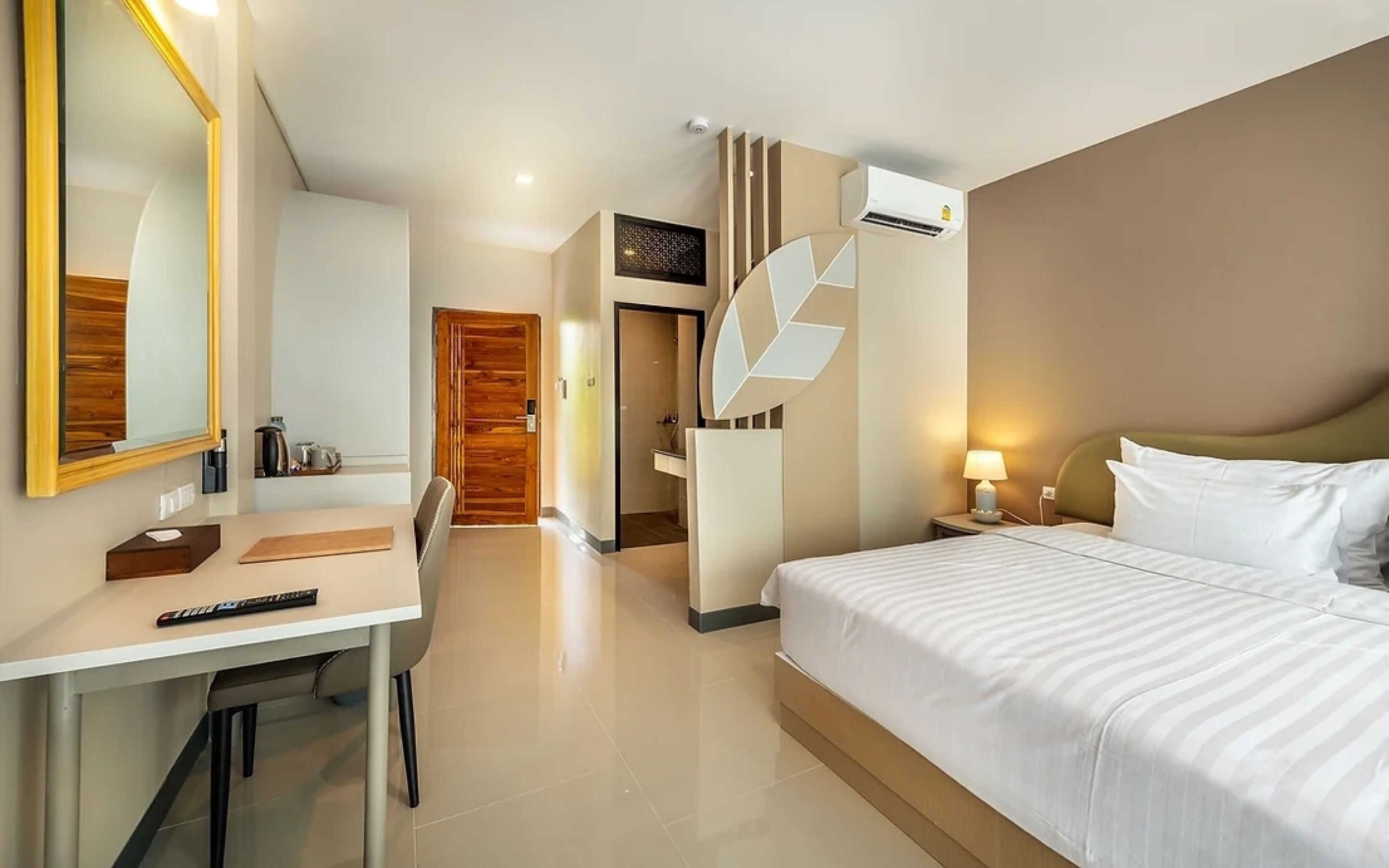 Quarto de hotel com cama, escrivaninha, cadeira e um espelho grande.
