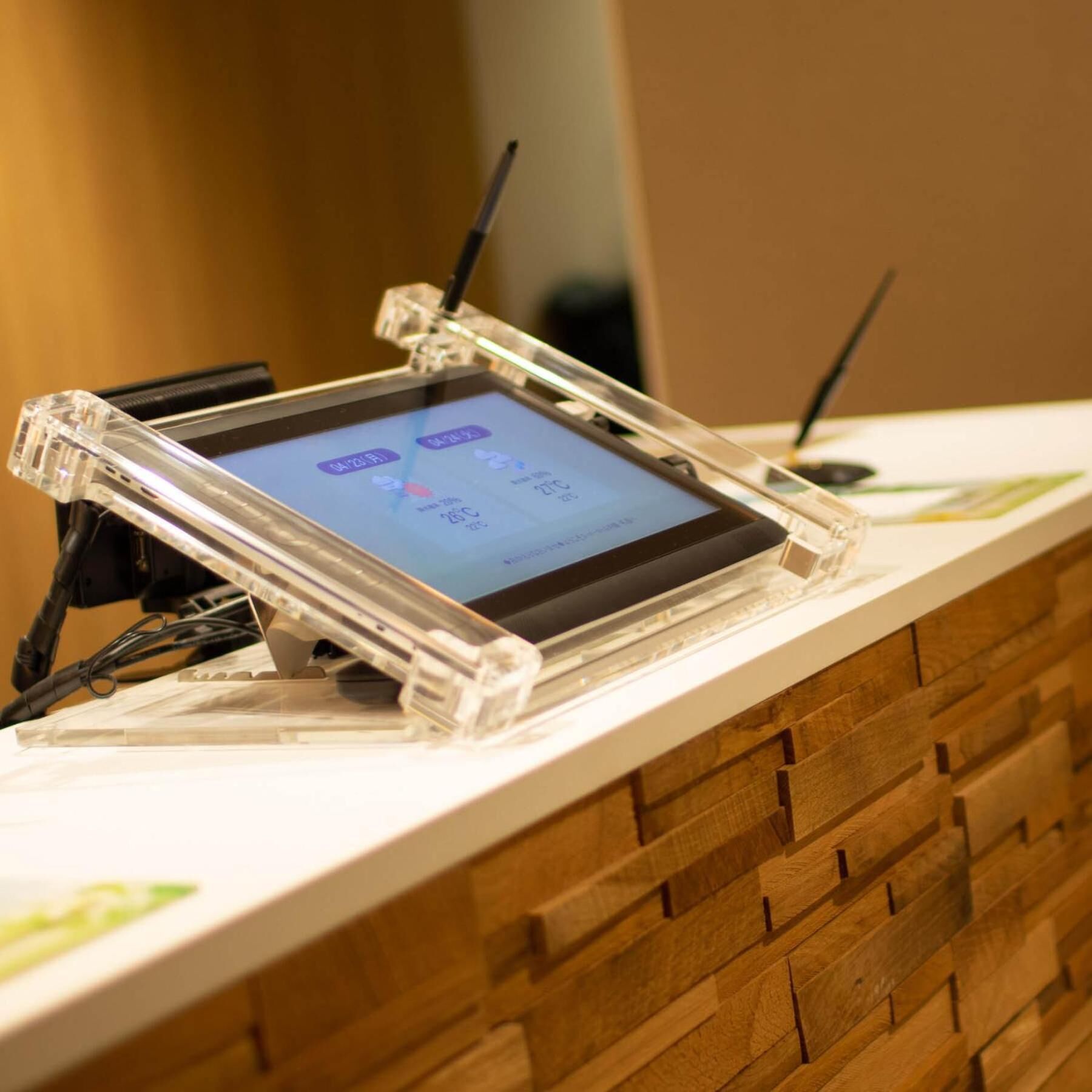 Um tablet sobre um suporte transparente, com um balcão de madeira e uma parede de tijolos.