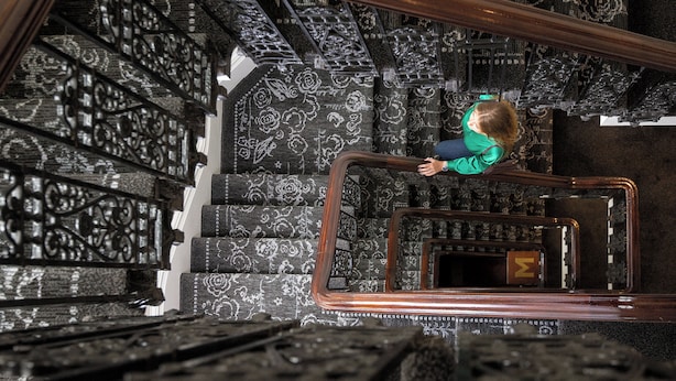 Escadaria com grades em preto e branco ricamente decoradas e corrimão de madeira.