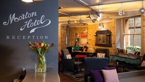 Uma área de recepção com uma placa indicando "Morton Hotel Reception", um vaso com tulipas e uma parede de tijolos ao fundo.
