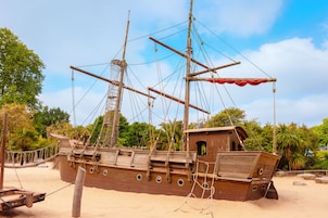 Um barco de madeira com cabine, ancorado em uma praia de areia com árvores ao fundo.