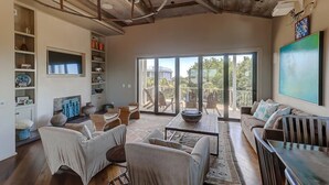 Uma sala de estar espaçosa com teto de madeira, uma ampla porta de vidro deslizante para uma varanda e uma moderna configuração de TV.