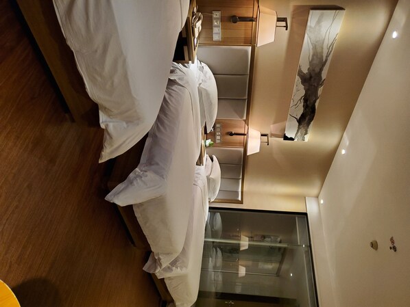 Quarto de hotel com cama, mesa de cabeceira, abajur e uma janela grande.