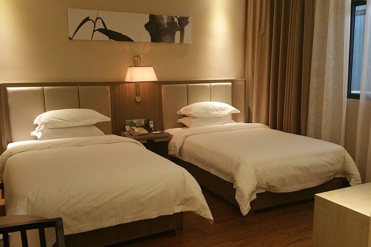 Quarto de hotel com duas camas, uma mesa de cabeceira com abajur e um quadro na parede.