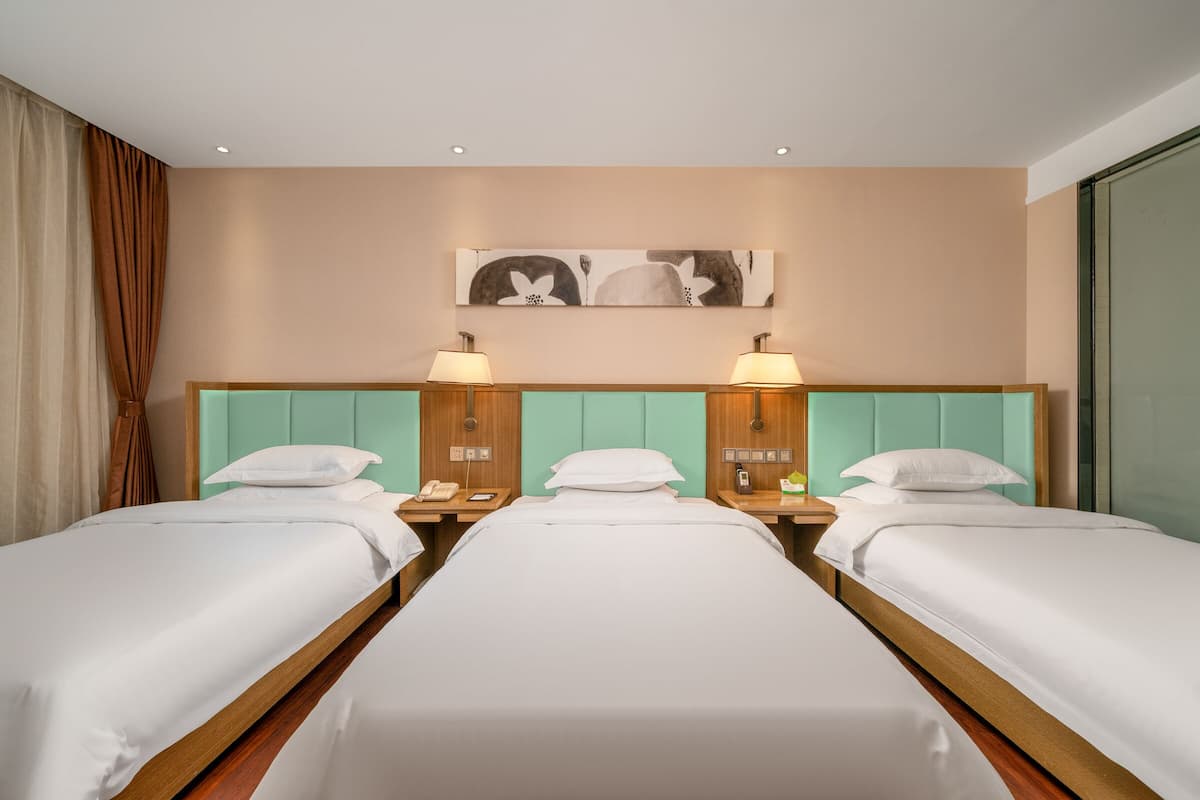 Quarto de hotel com duas camas de solteiro, cabeceira verde-água, luminárias de cabeceira e uma obra de arte pendurada na parede.