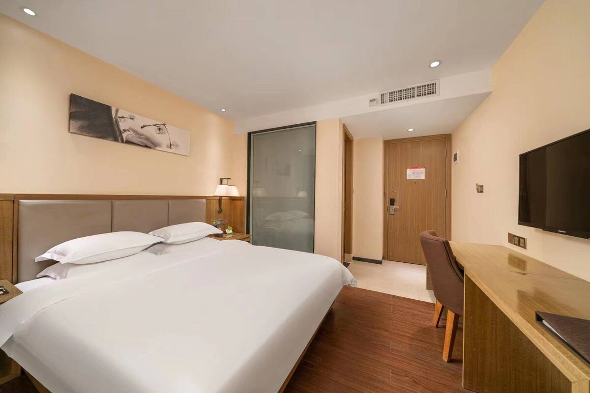 Quarto de hotel com cama, escrivaninha, cadeira, televisão e porta.