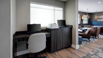Um espaço de escritório moderno com uma mesa, computador e impressora. Há uma área de estar com mesas e cadeiras.