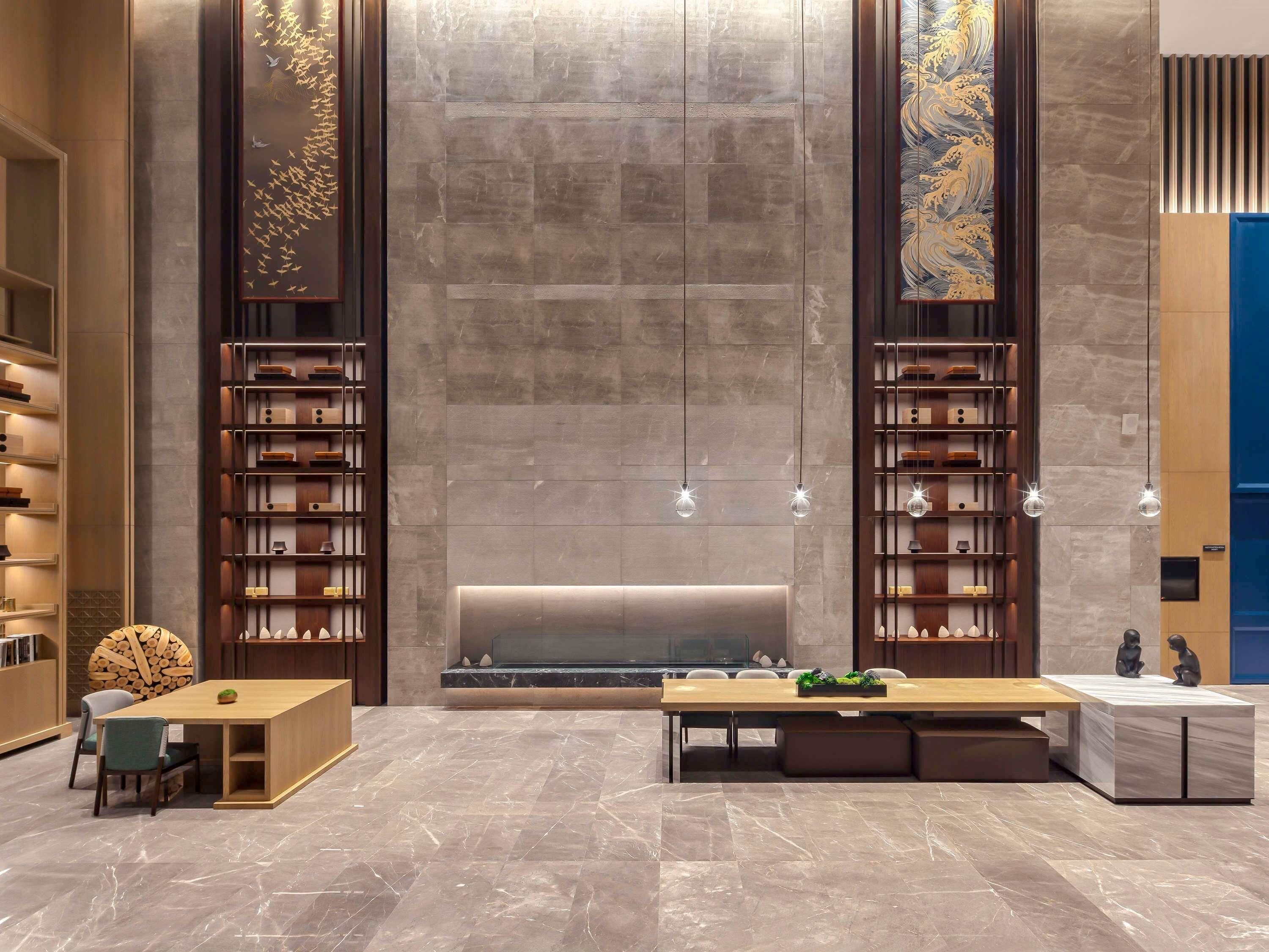 Um lobby moderno com piso de mármore, um balcão de recepção e duas grandes estantes com painéis decorativos.