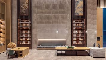 Um lobby moderno com piso de mármore, um balcão de recepção e duas grandes estantes com painéis decorativos.