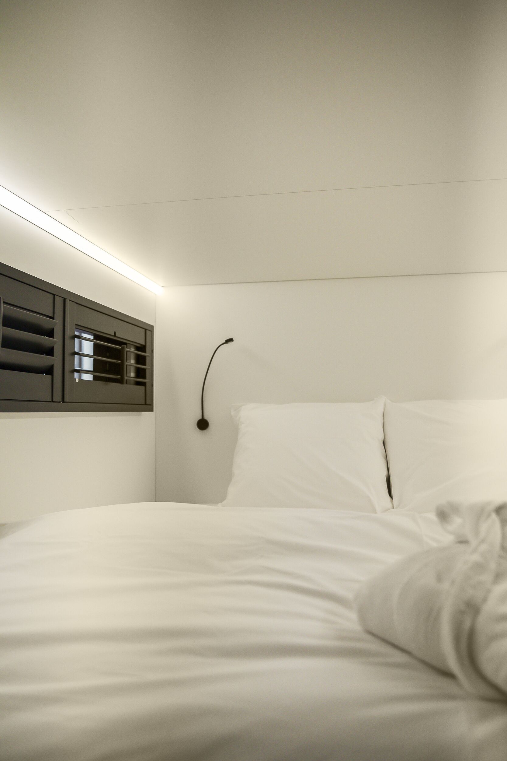 Cama bem arrumada em quarto com design moderno, incluindo prateleira fixada na parede e luminária de parede singular.