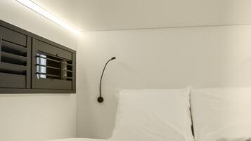 Cama bem arrumada em quarto com design moderno, incluindo prateleira fixada na parede e luminária de parede singular.