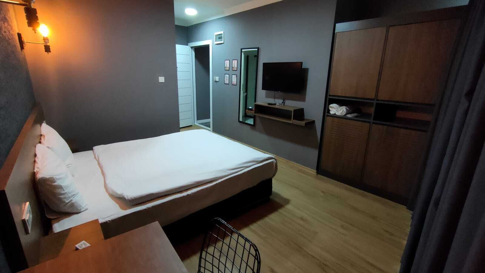 Quarto de hotel com cama, escrivaninha, televisão e guarda-roupa.