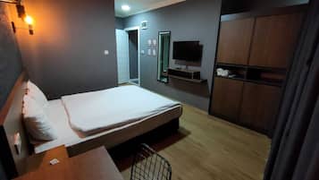 Quarto de hotel com cama, escrivaninha, televisão e guarda-roupa.
