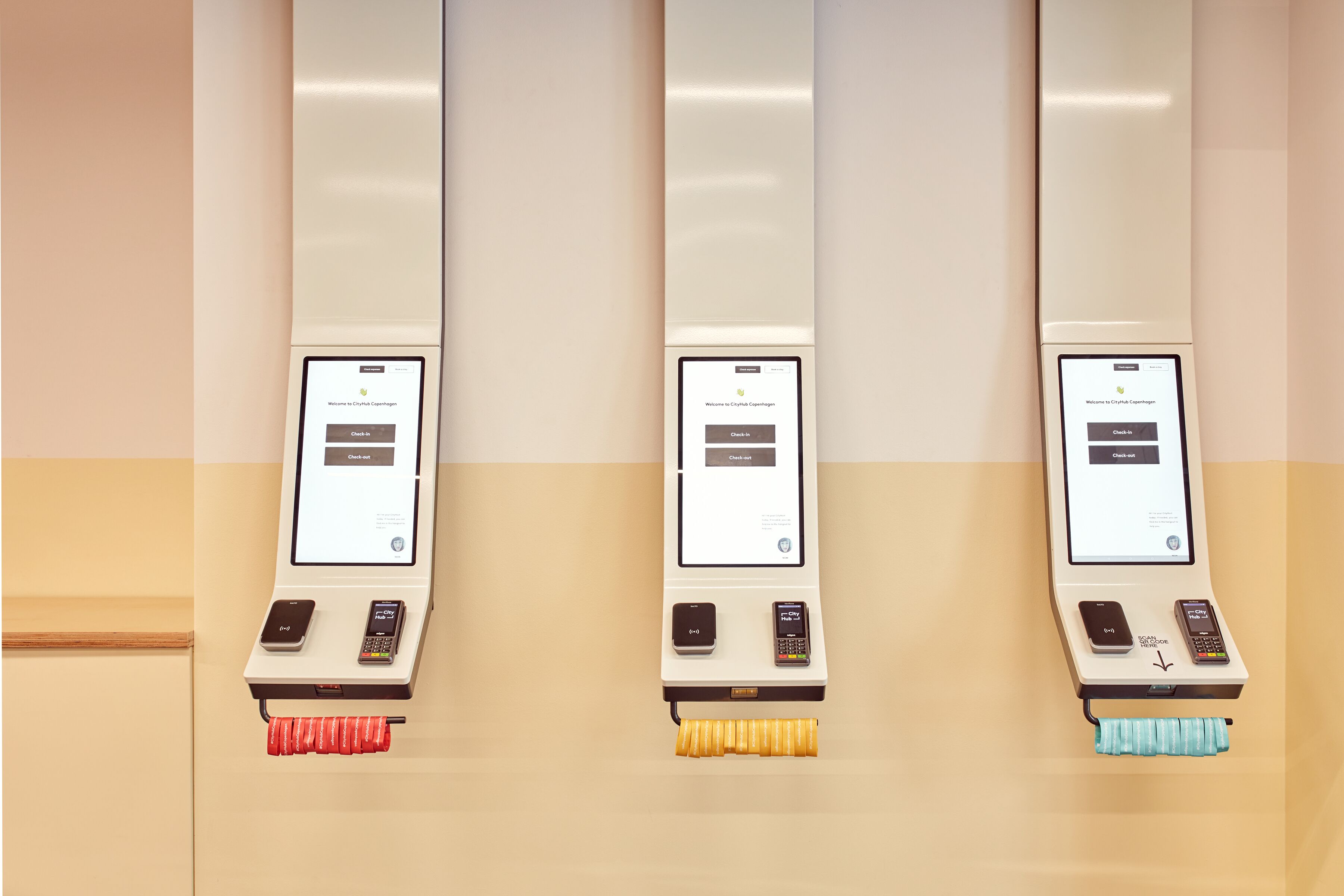 Três totens de autoatendimento com telas e leitores de cartão, cada um com um telefone e um caixa eletrônico.