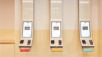 Três totens de autoatendimento com telas e leitores de cartão, cada um com um telefone e um caixa eletrônico.