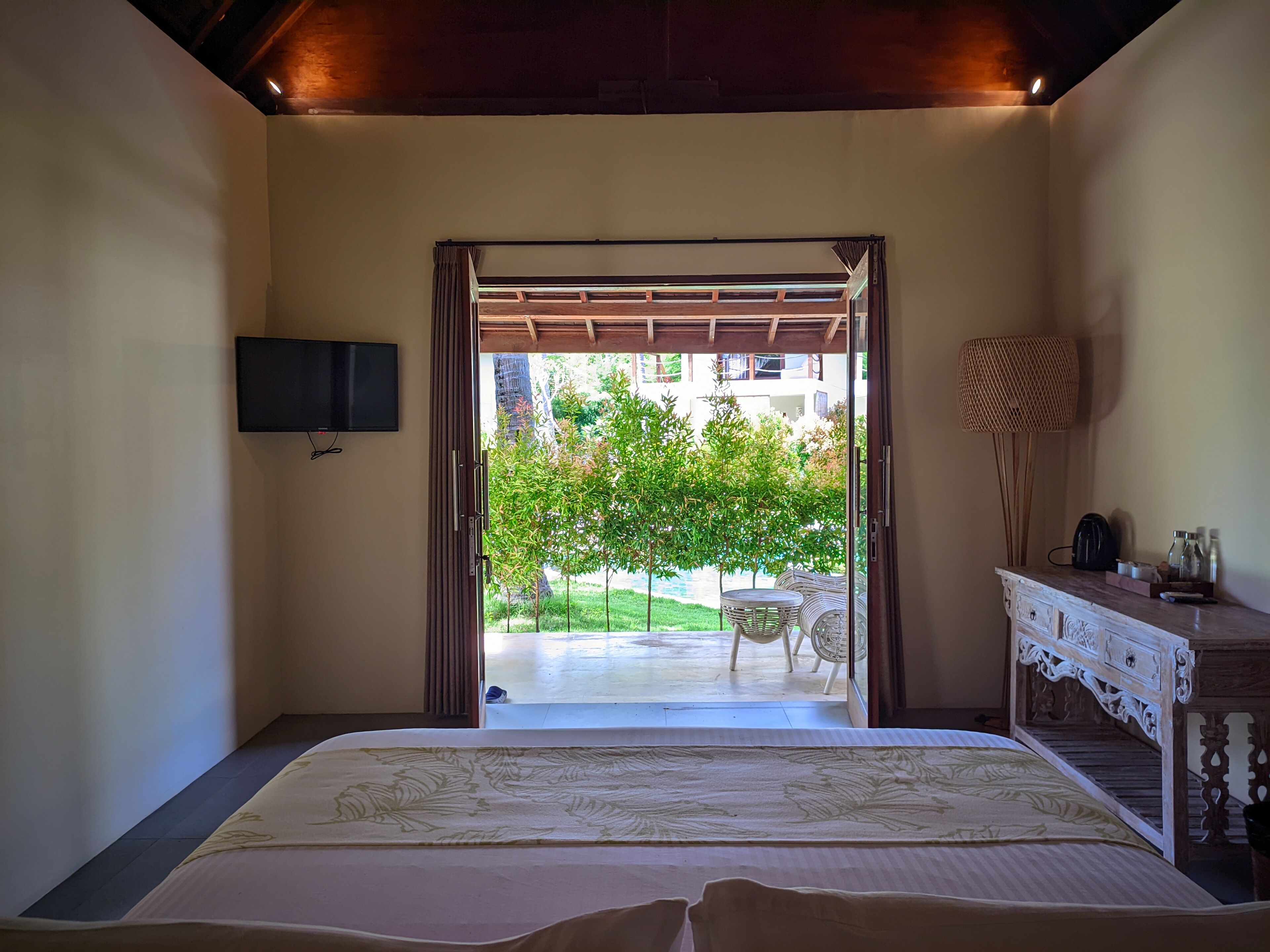 Quarto com cama, televisão, penteadeira e vista para um jardim por uma porta aberta.