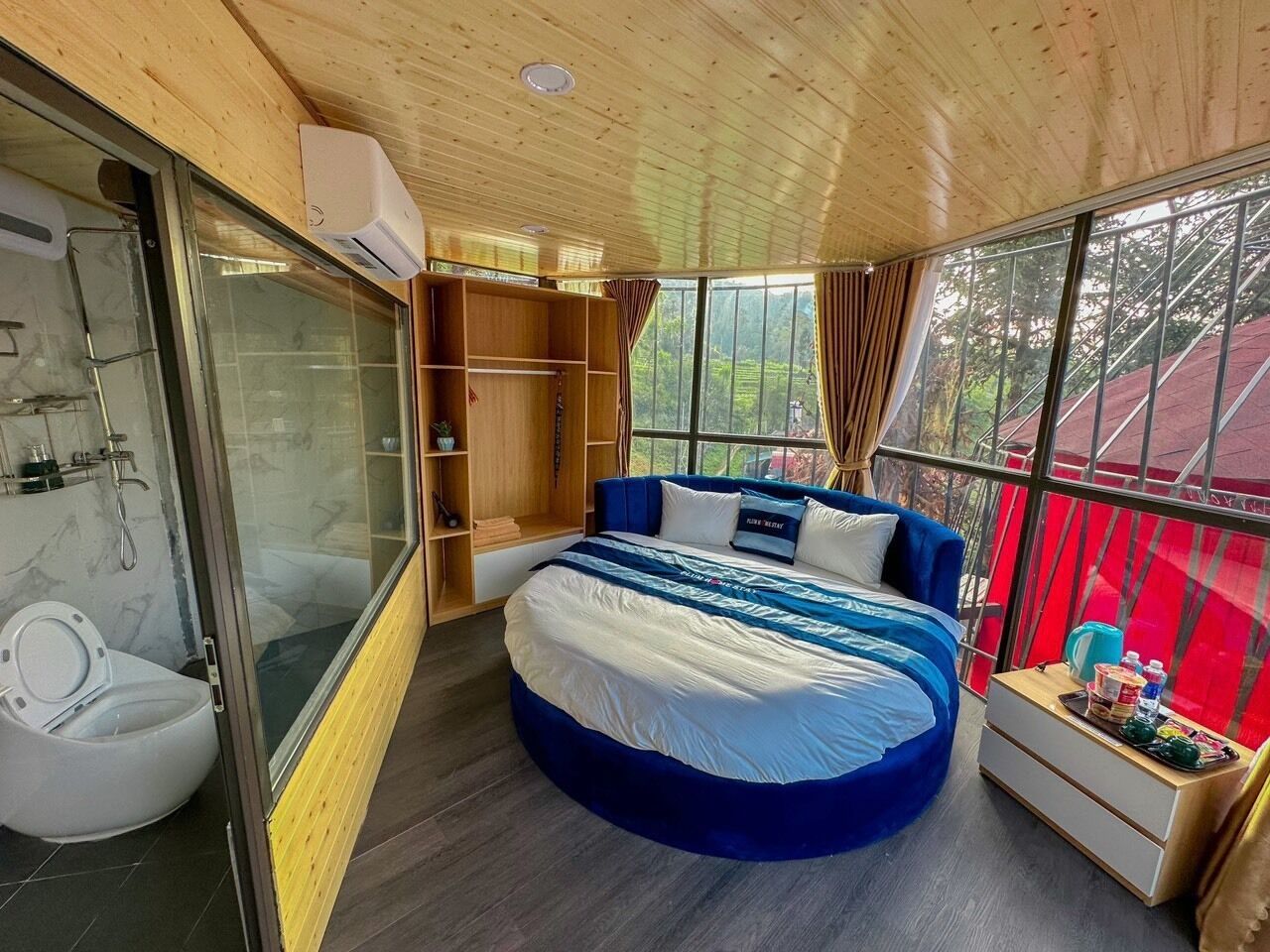 Quarto com cama grande, guarda-roupa de madeira, cabine de chuveiro em vidro e vista para o exterior.