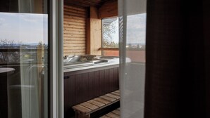 Uma cabana de madeira com hidromassagem, um banco de madeira e uma vista pela janela.