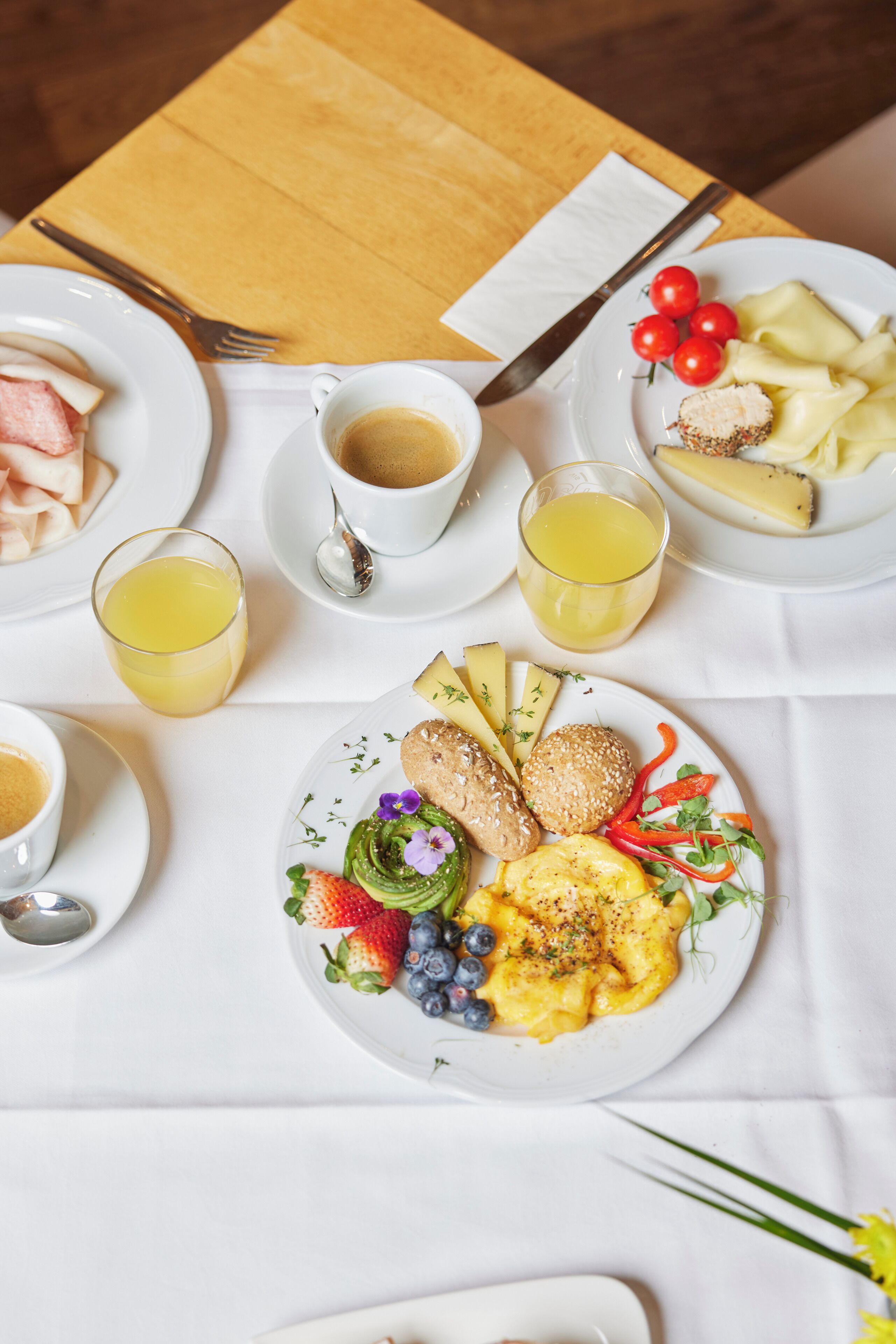 Mesa de café da manhã com pratos de comida, xícaras de café e copos de suco.