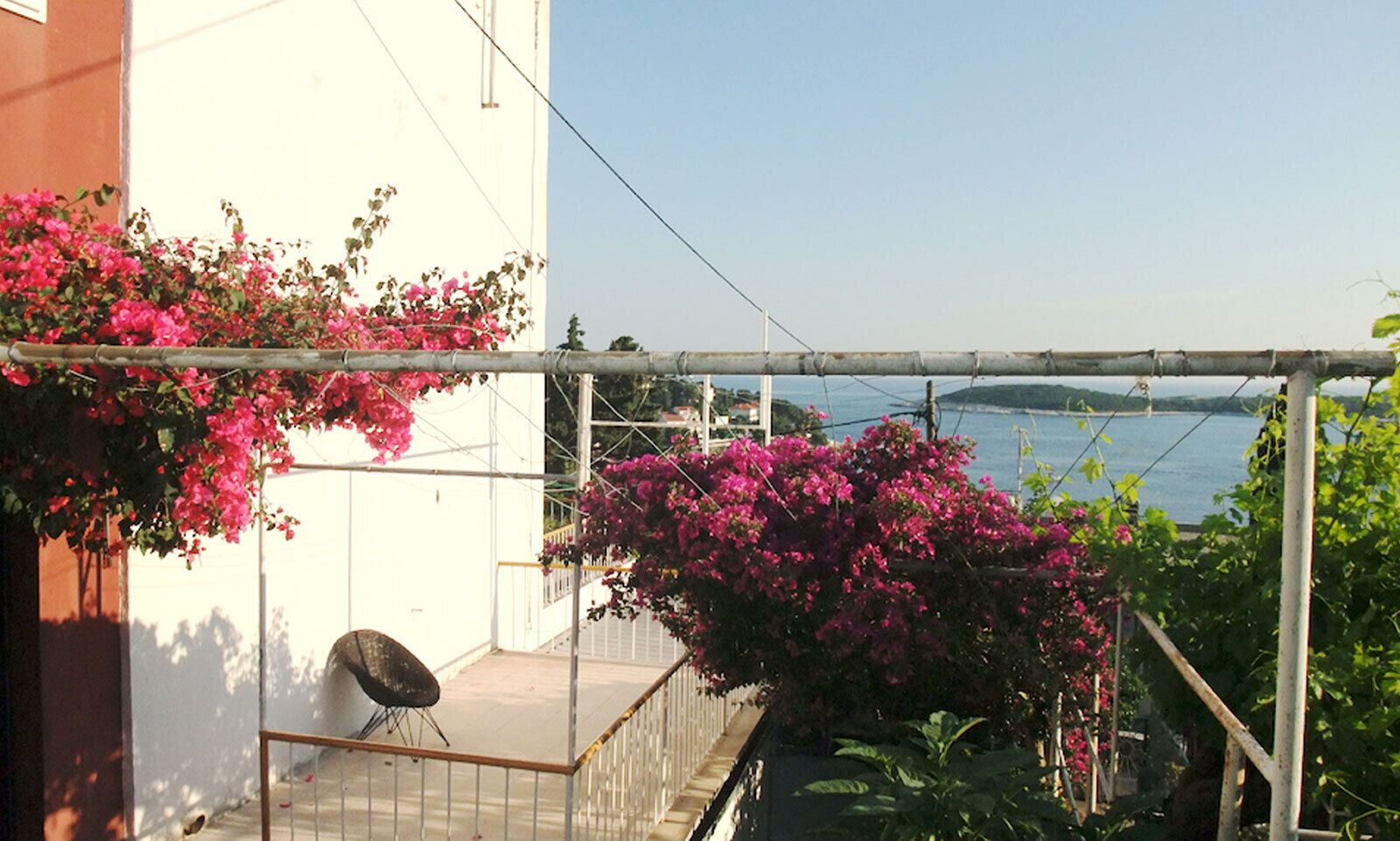 Uma varanda com vista para o mar, uma cadeira e plantas de buganvillea rosa.