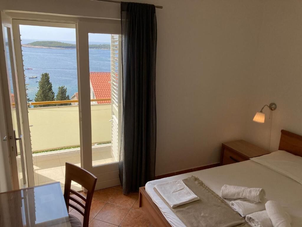 Quarto de hotel com cama, escrivaninha e vista para o mar através de uma porta deslizante.