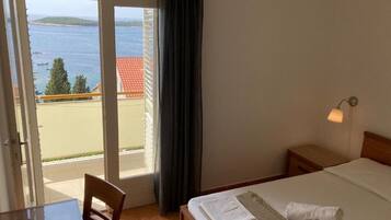 Quarto de hotel com cama, escrivaninha e vista para o mar através de uma porta deslizante.