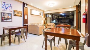 Uma área de refeições com uma mesa e cadeiras de madeira, um sofá e uma cozinha visível através de uma porta de vidro.
