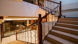 Uma escadaria com grades de metal ornamentadas e balaústres de madeira, levando a um andar superior.