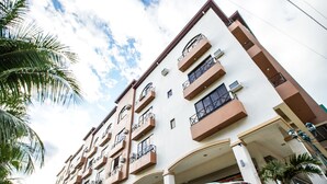 Um edifício de vários andares com varandas, aparelhos de ar condicionado e um carro estacionado em frente.