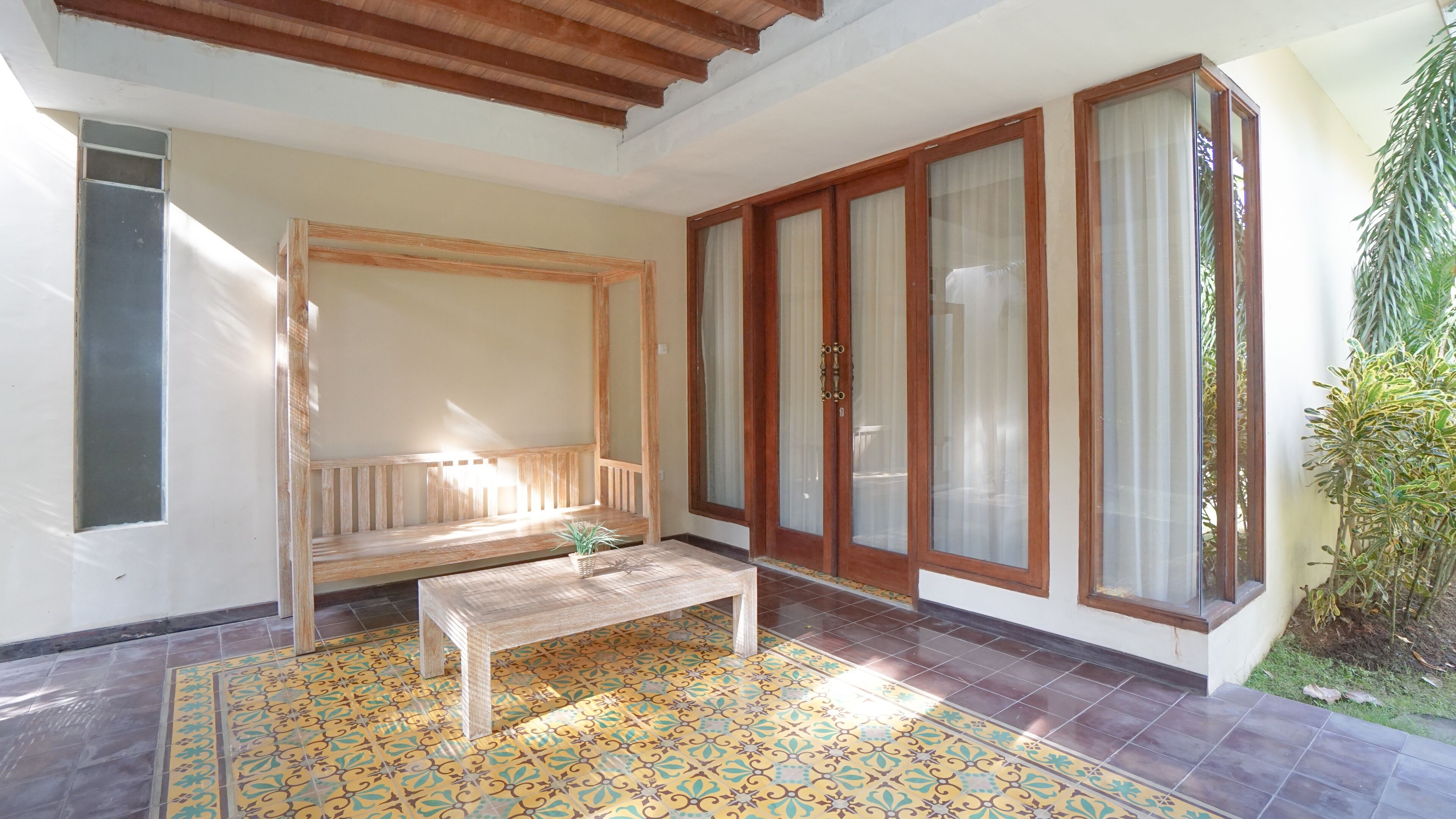 Um quarto com um banco de madeira, uma pequena mesa e uma grande porta de madeira com painéis de vidro.