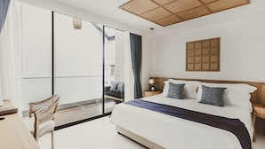 Quarto de hotel moderno com uma cama grande, uma cadeira, uma mesinha de cabeceira e vista através de uma porta de vidro.