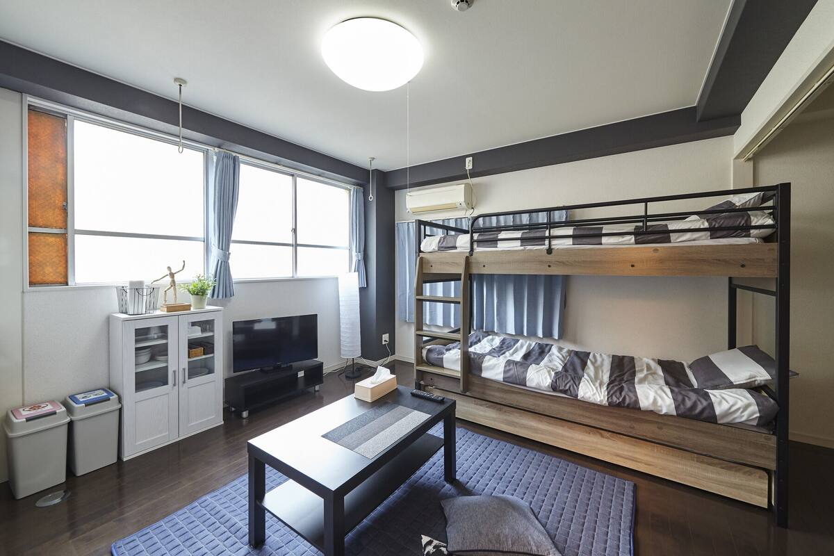 Quarto compacto com beliches, televisão, armário pequeno e janela com cortinas.
