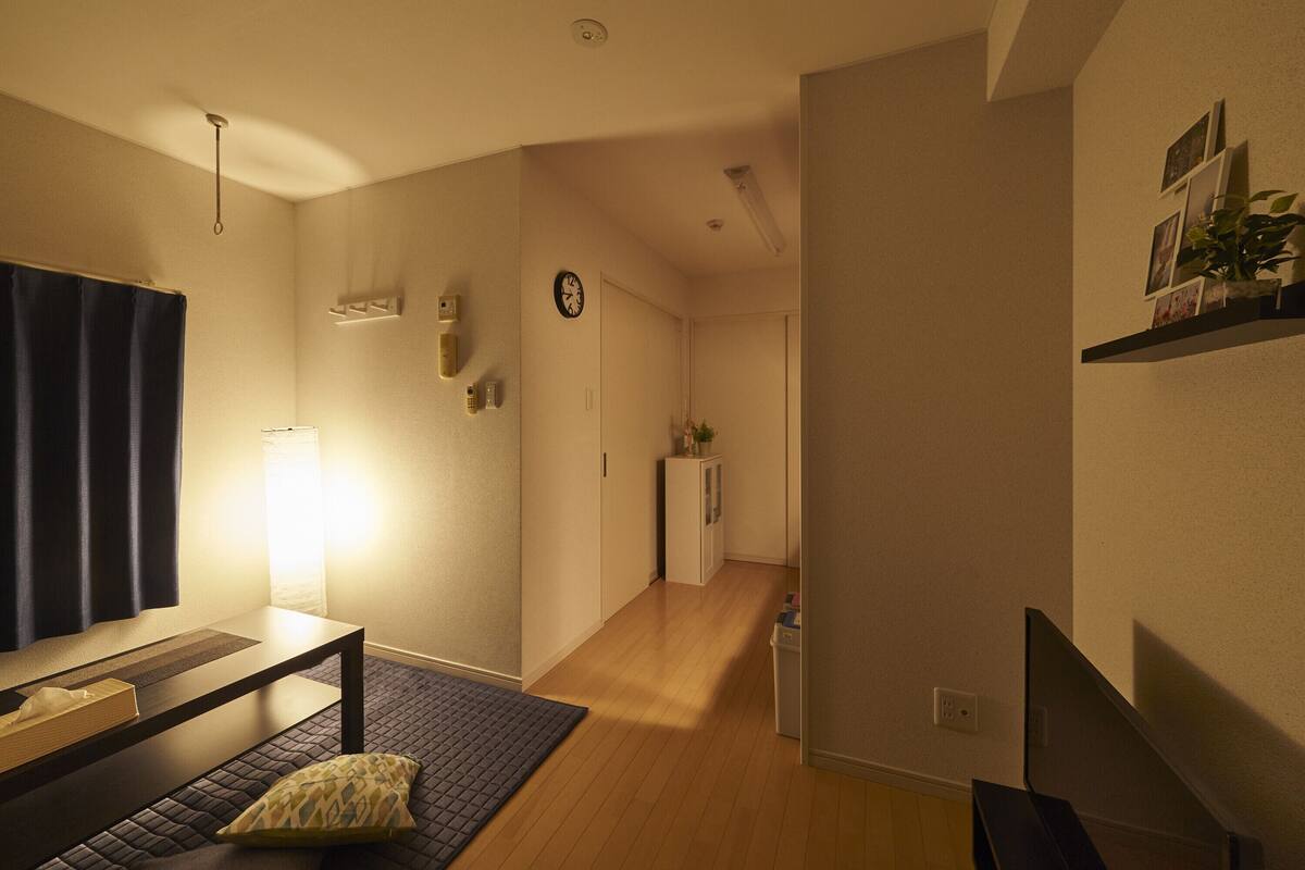 Espaço compacto com sofá, uma mesinha, abajur, relógio e estante com fotografias.