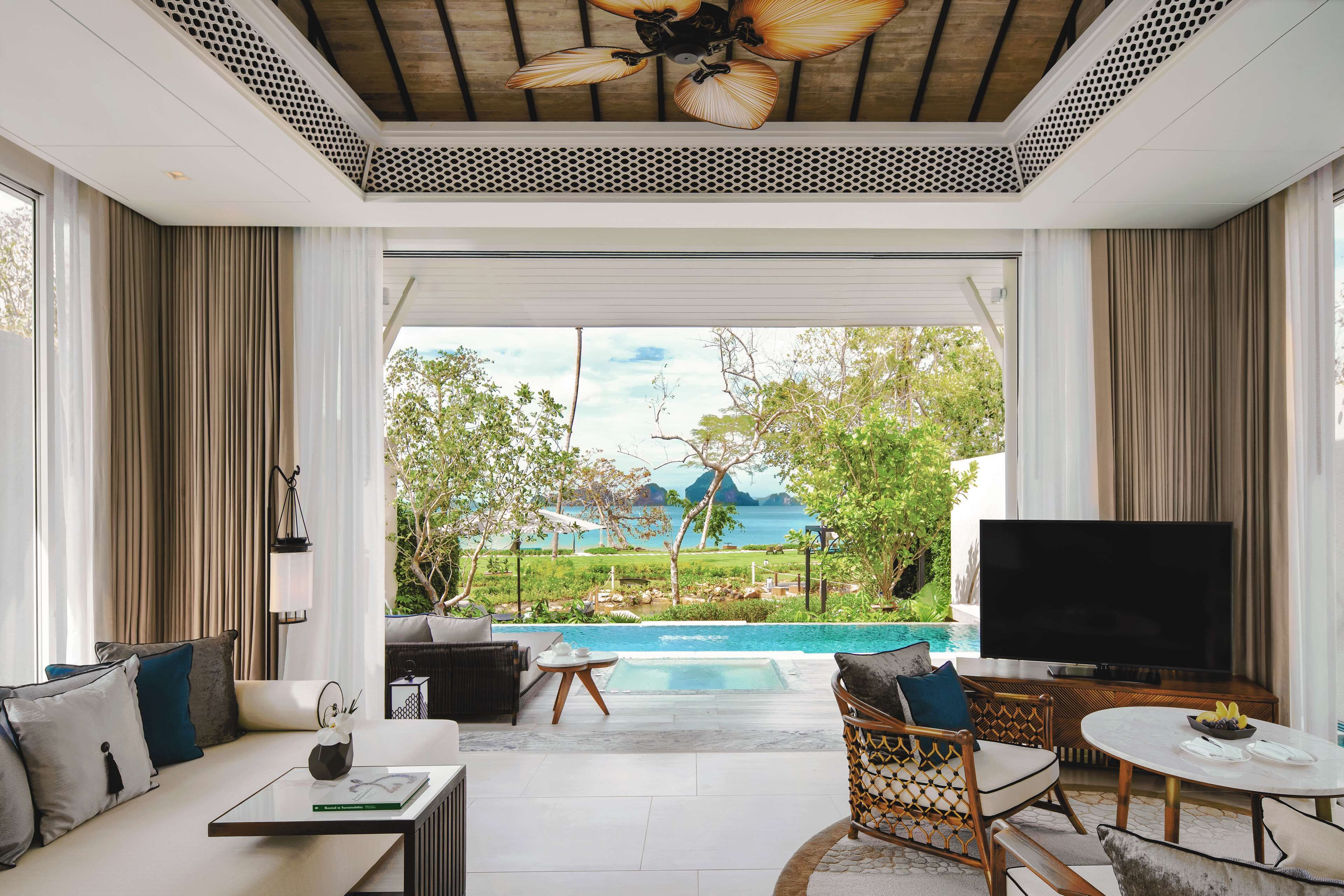 Ampla sala de estar com uma televisão grande, assentos confortáveis e vista para uma piscina e vegetação.