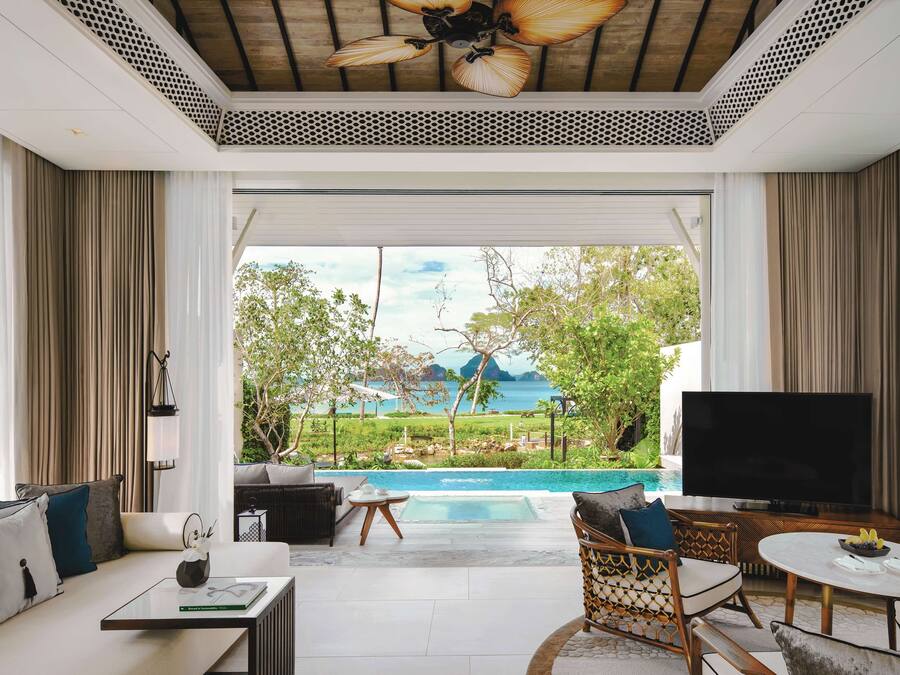 Ampla sala de estar com uma televisão grande, assentos confortáveis e vista para uma piscina e vegetação.