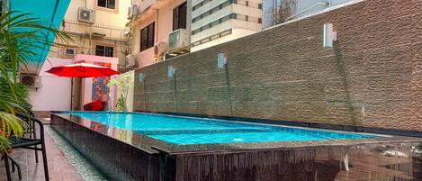 Piscina ao ar livre com parede de pedra e um guarda-sol vermelho.