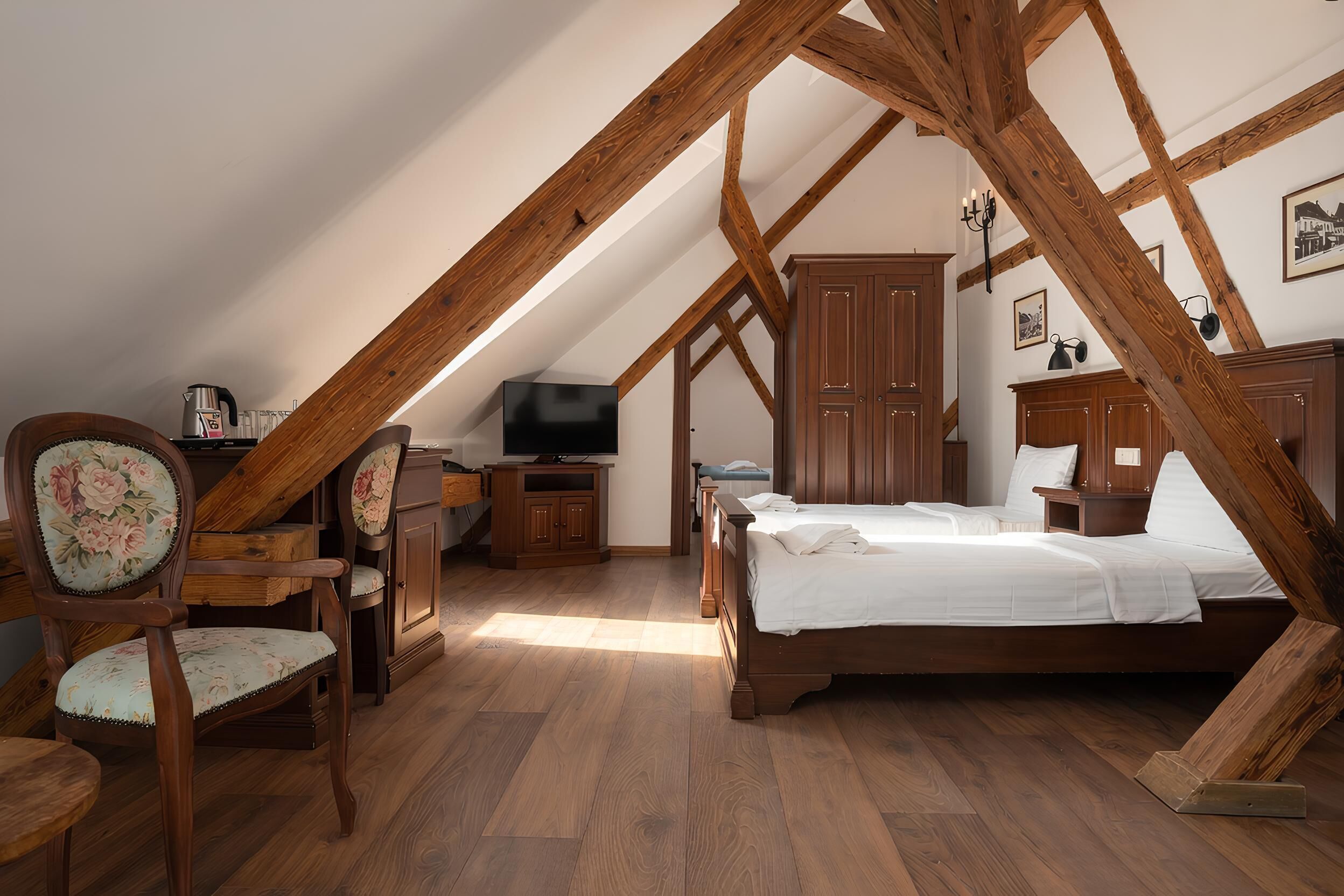 Quarto com teto inclinado, vigas de madeira, cama, escrivaninha, cadeira e televisão.