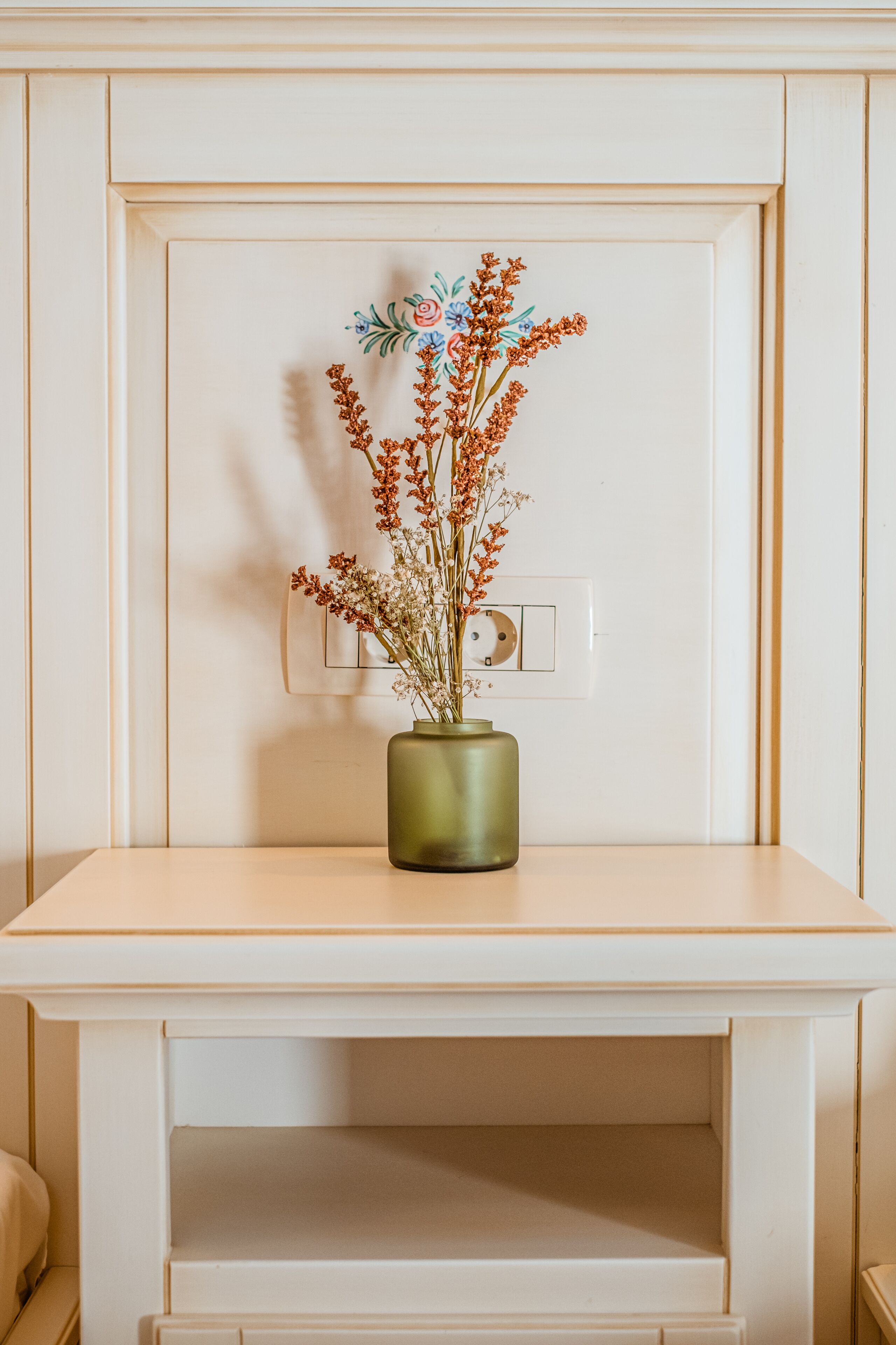 Um aparador branco com um vaso verde contendo flores secas.