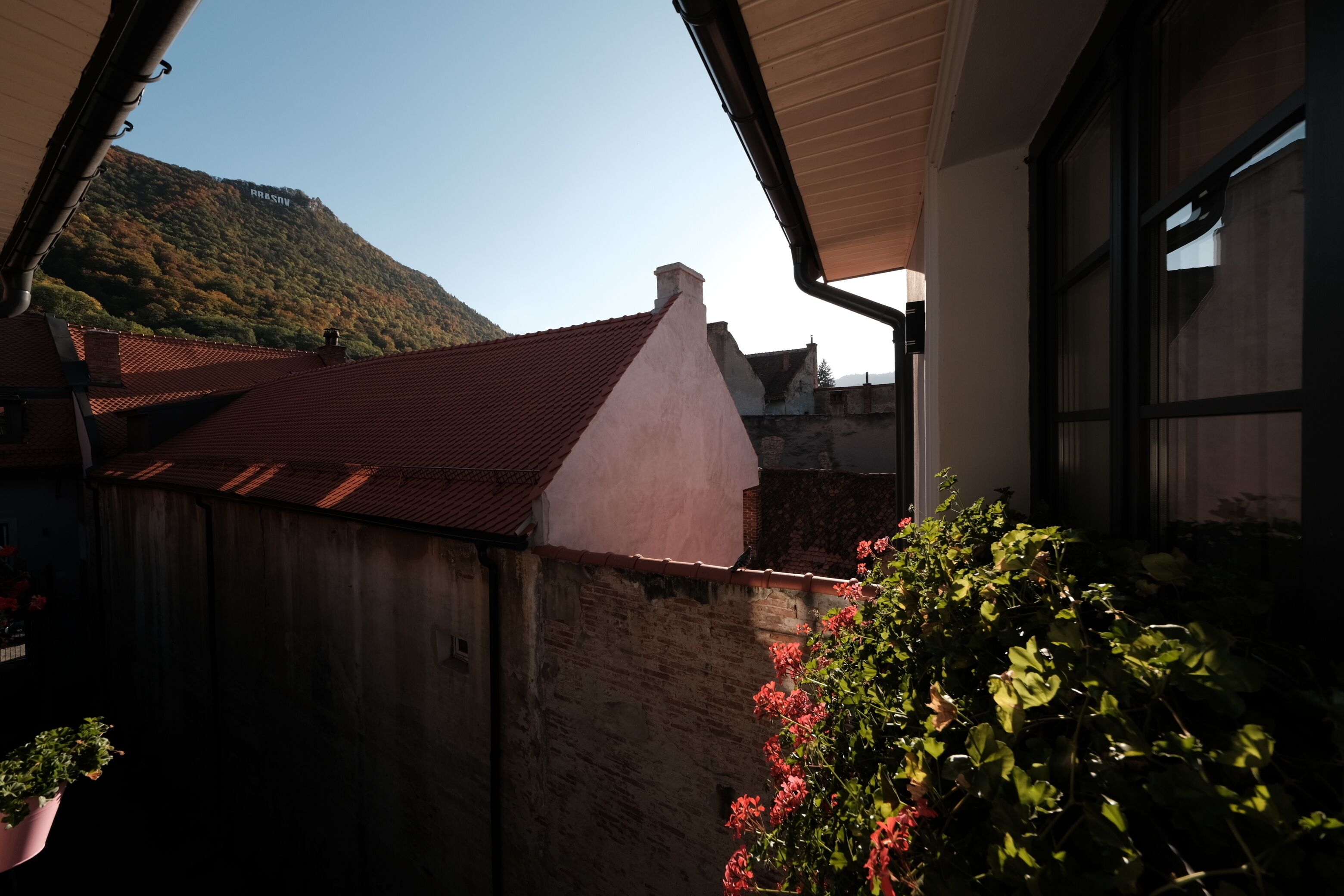 Um edifício com telhado de telhas vermelhas, uma parede de pedra e vista para uma colina com a palavra 
