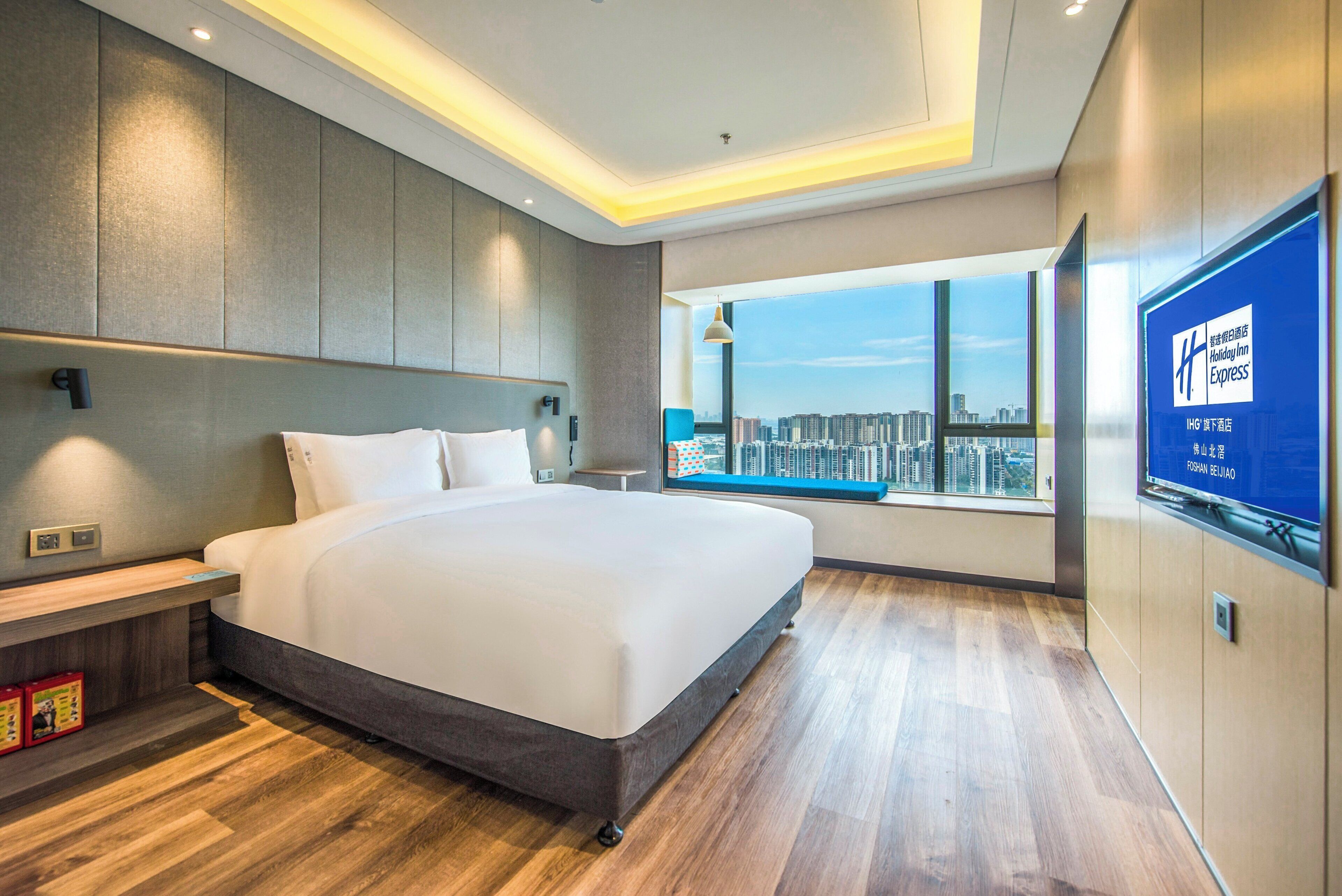 Quarto de hotel moderno com uma cama grande, vista para a cidade e televisão na parede.