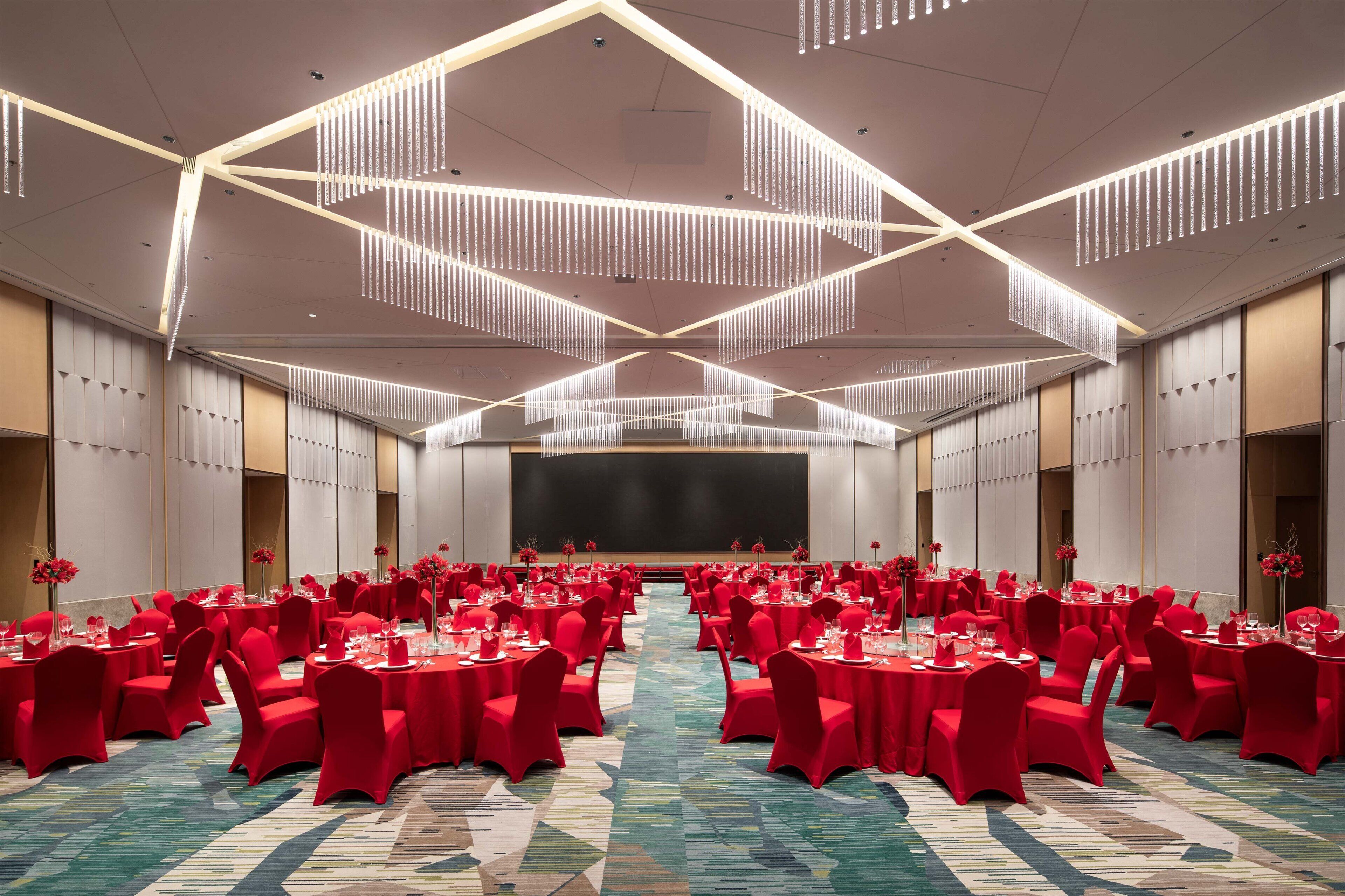 Ampla sala de conferências com mesas preparadas para um evento formal, apresentando um design de teto moderno com luminárias lineares.
