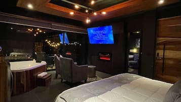Quarto moderno com uma cama grande, uma televisão e um pequeno espaço de estar com uma poltrona e uma mesa.