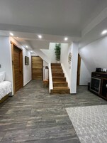 Um interior moderno com escada de madeira, um sofá branco, um banquinho pequeno e uma área de cozinha.