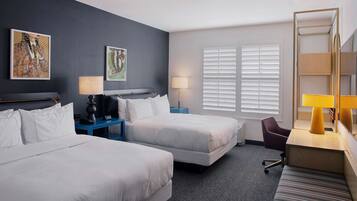 Quarto de hotel com duas camas, uma escrivaninha, uma cadeira e um espelho grande.