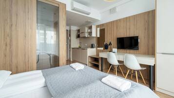 Quarto de hotel moderno com uma cama, uma escrivaninha, duas cadeiras, uma televisão e um espaço de cozinha equipado.