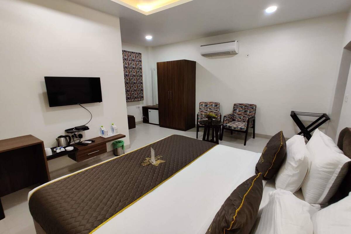 Quarto de hotel com cama, televisão, guarda-roupa, secretária com chaleira e uma cadeira.