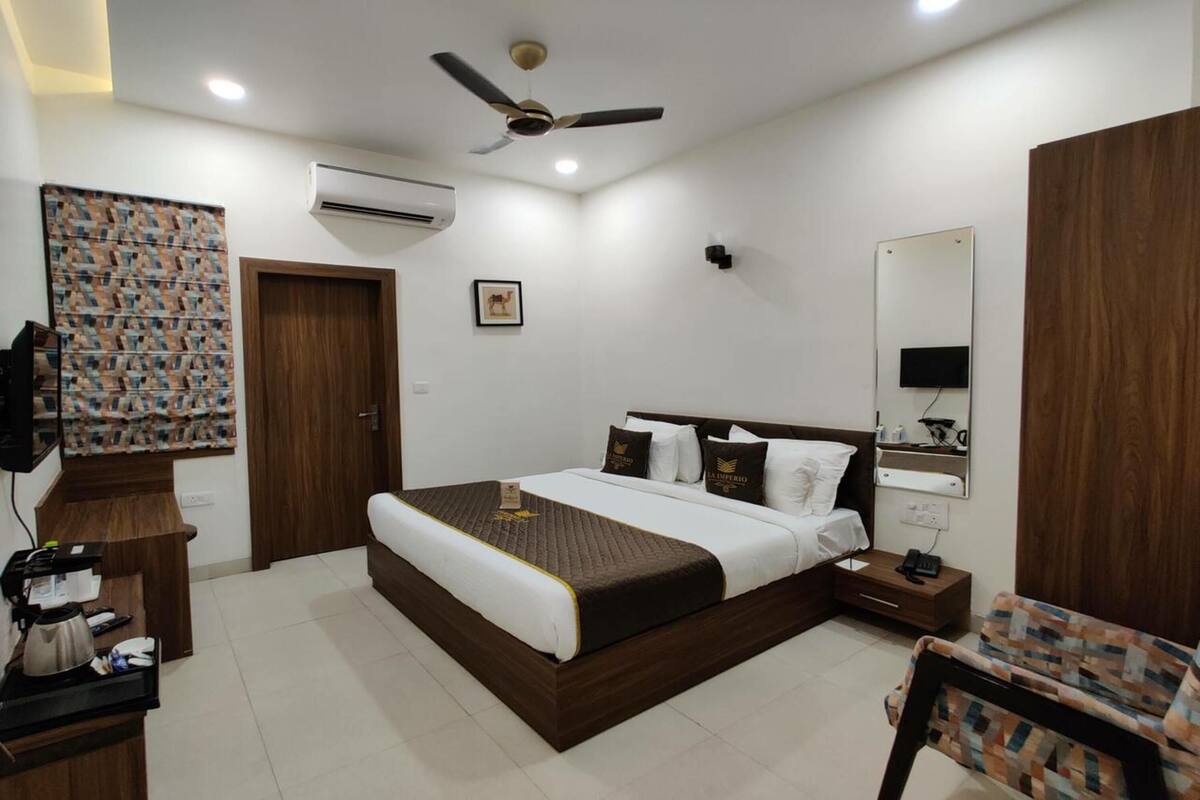 Quarto de hotel com cama, escrivaninha, cadeira, ventilador de teto, ar condicionado, espelho e parede com design estampado.