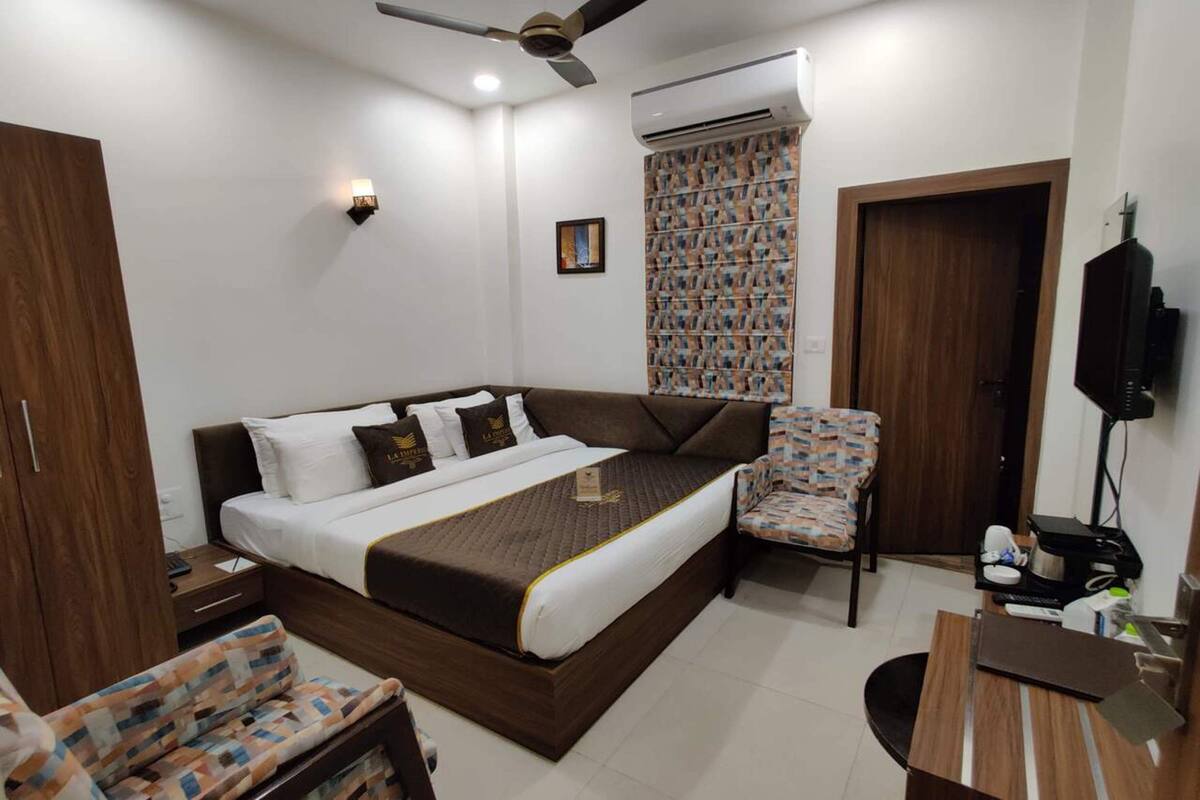 Quarto de hotel com cama, uma cadeira, escrivaninha, ar condicionado, televisão e guarda-roupa.