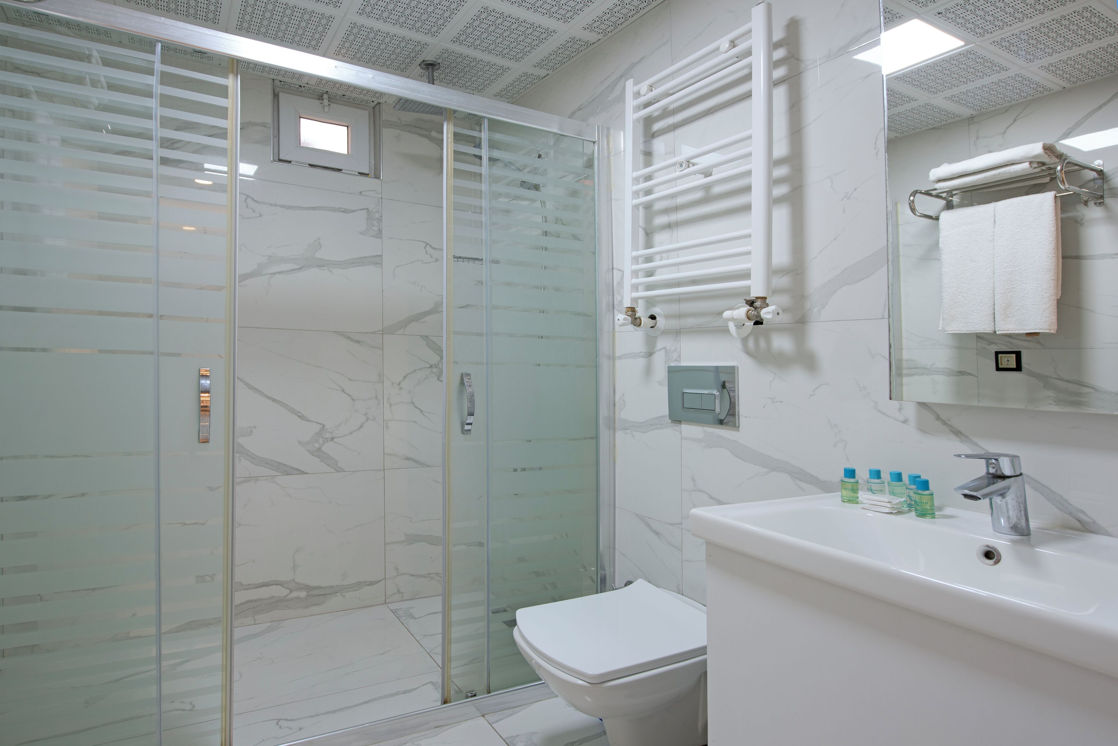 Um banheiro moderno com chuveiro em gabinete de vidro, vaso sanitário branco e pia com amenities.