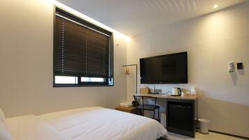 Quarto de hotel com cama, escrivaninha com computador, televisão e uma pequena cozinha.